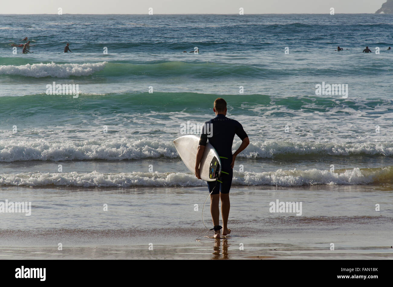 A surfboard rider walks to the waters edge on a sunny morning at ...