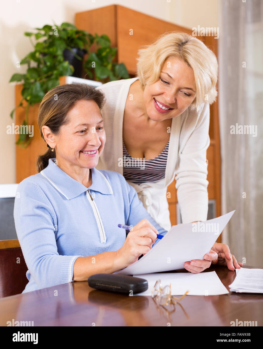 Smiling mature ladies signing documents at home. Focus on the woman on ...
