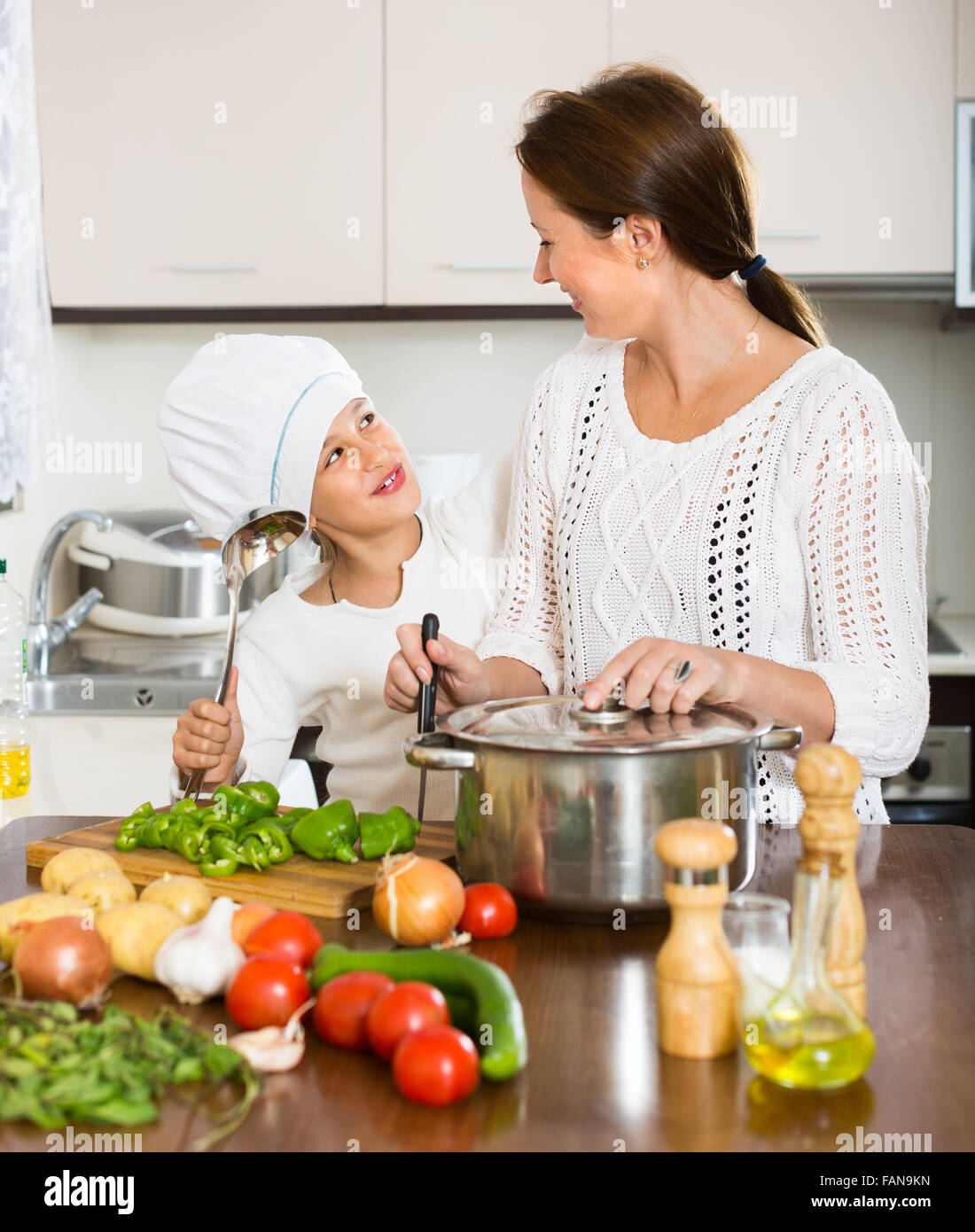 Cheerful mother and her preschooler daughter preparing soup at domestic ...