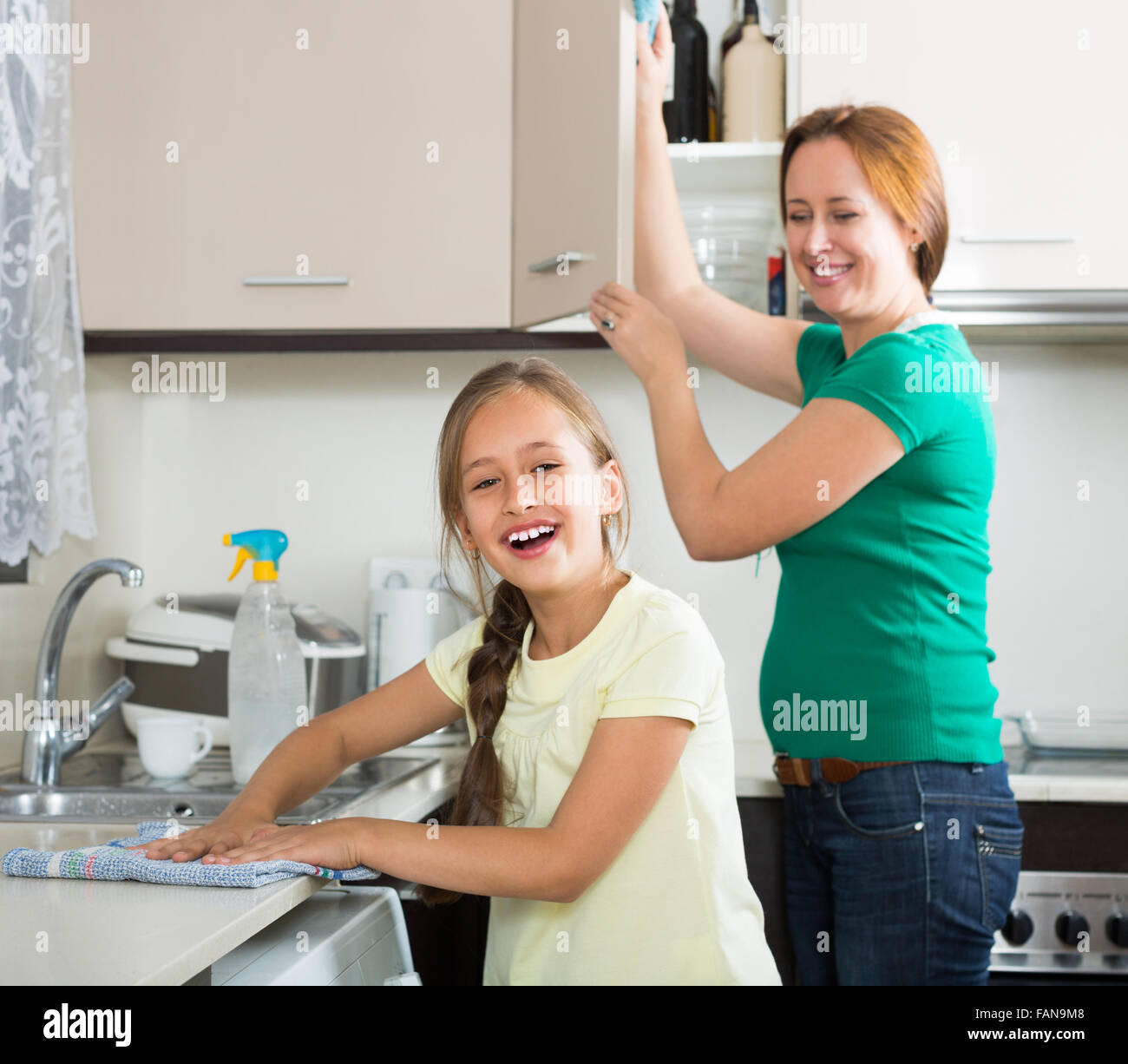 Happy smiling girl helping mother dusting furniture indoor. Focus on ...