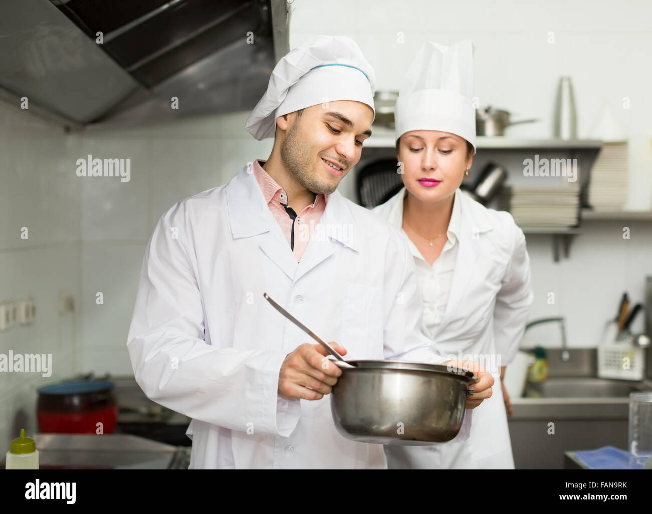 Two positive professional cooks working together at restaurant kitchen ...