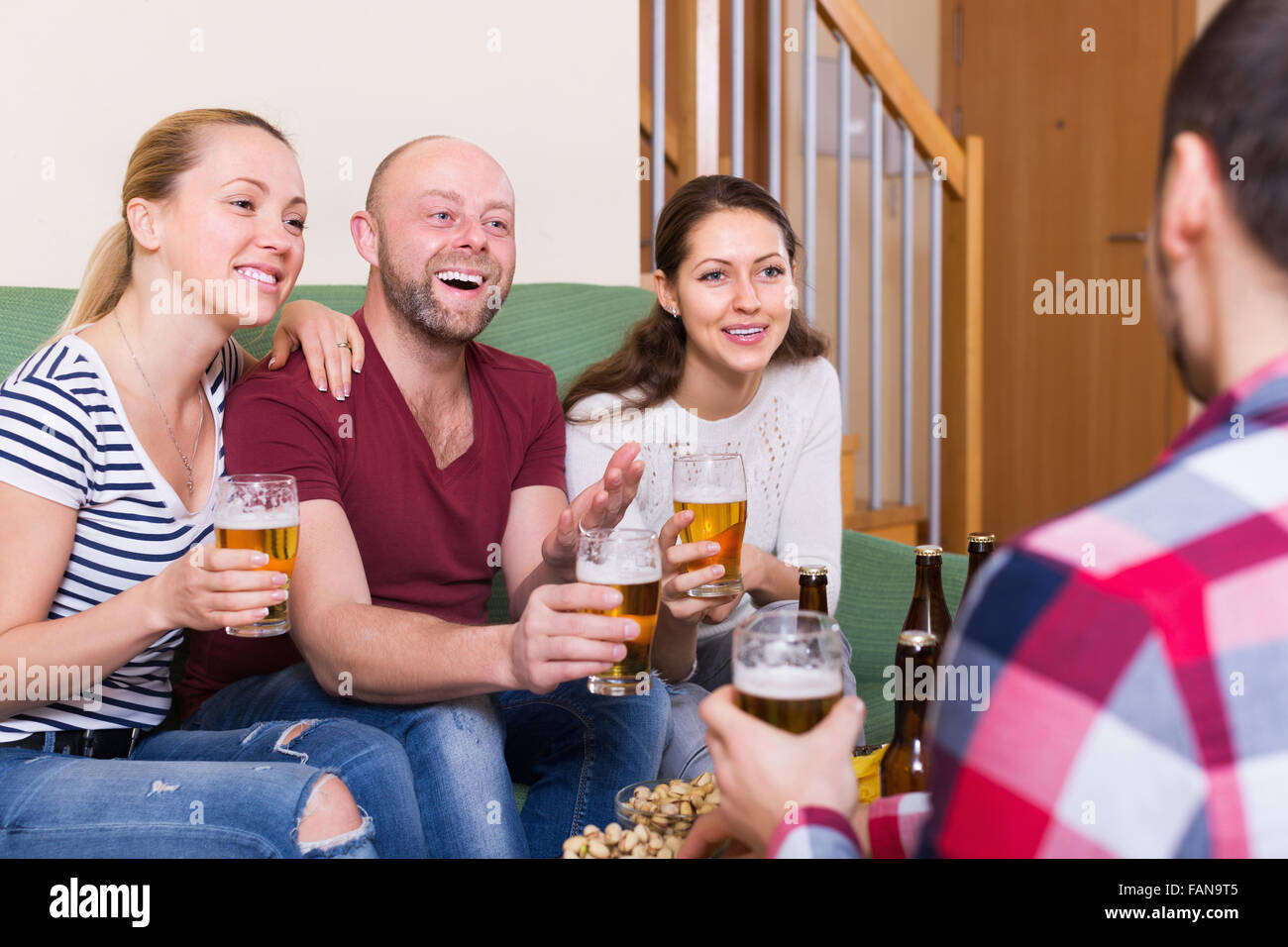 Two smiling adults couples hanging out with beer and snacks at at house ...