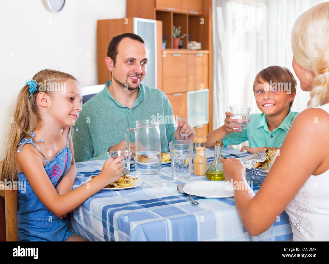 Friendly mother, father and kids sitting at the table at a home and ...