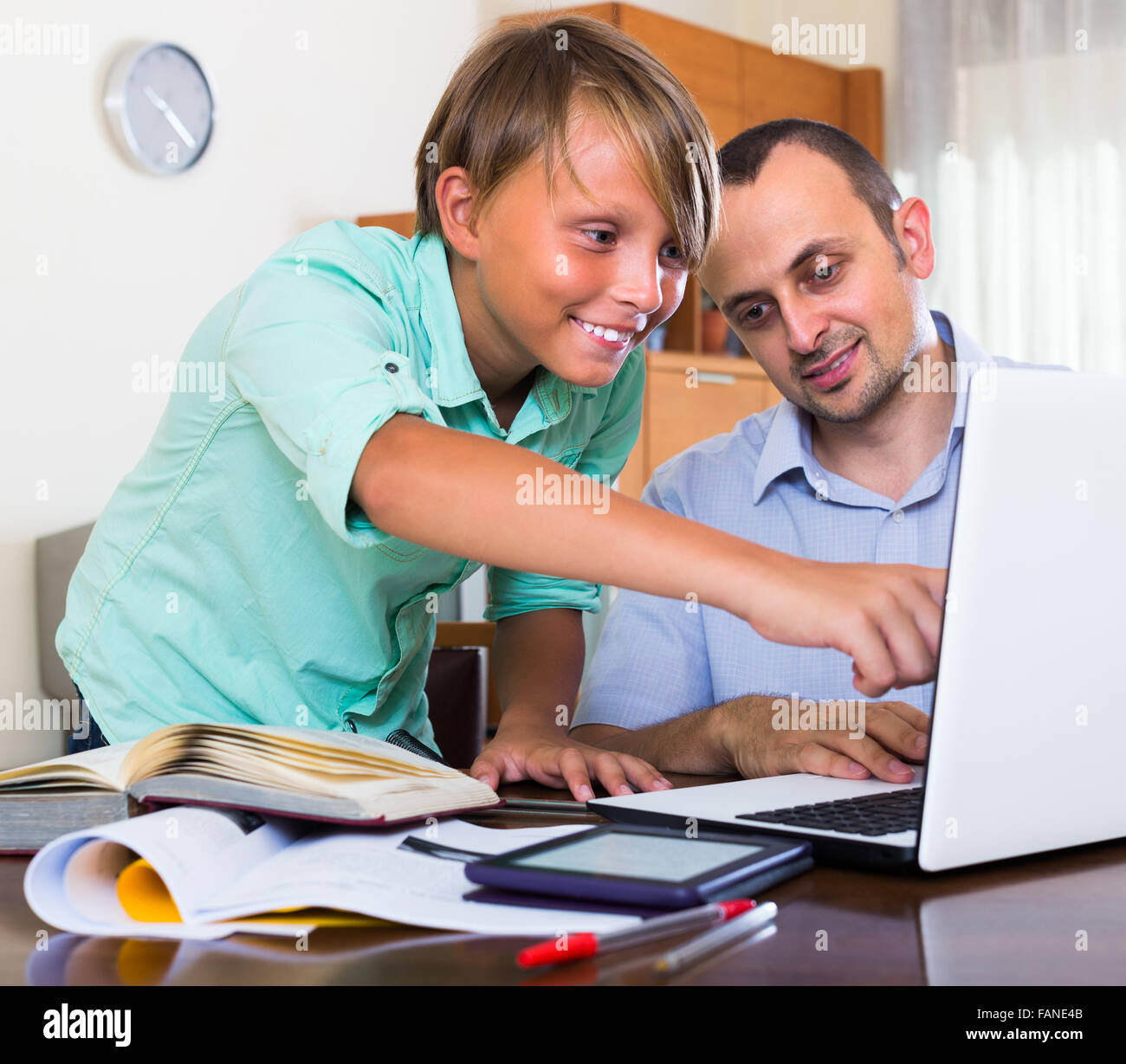 Positive man helping joyful teenage son to do homework at home Stock ...