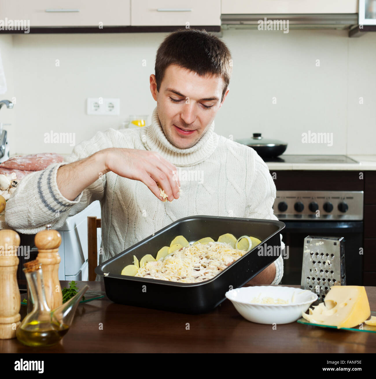 Smiling guy cooking french-style meat. Adding grating cheese in ...