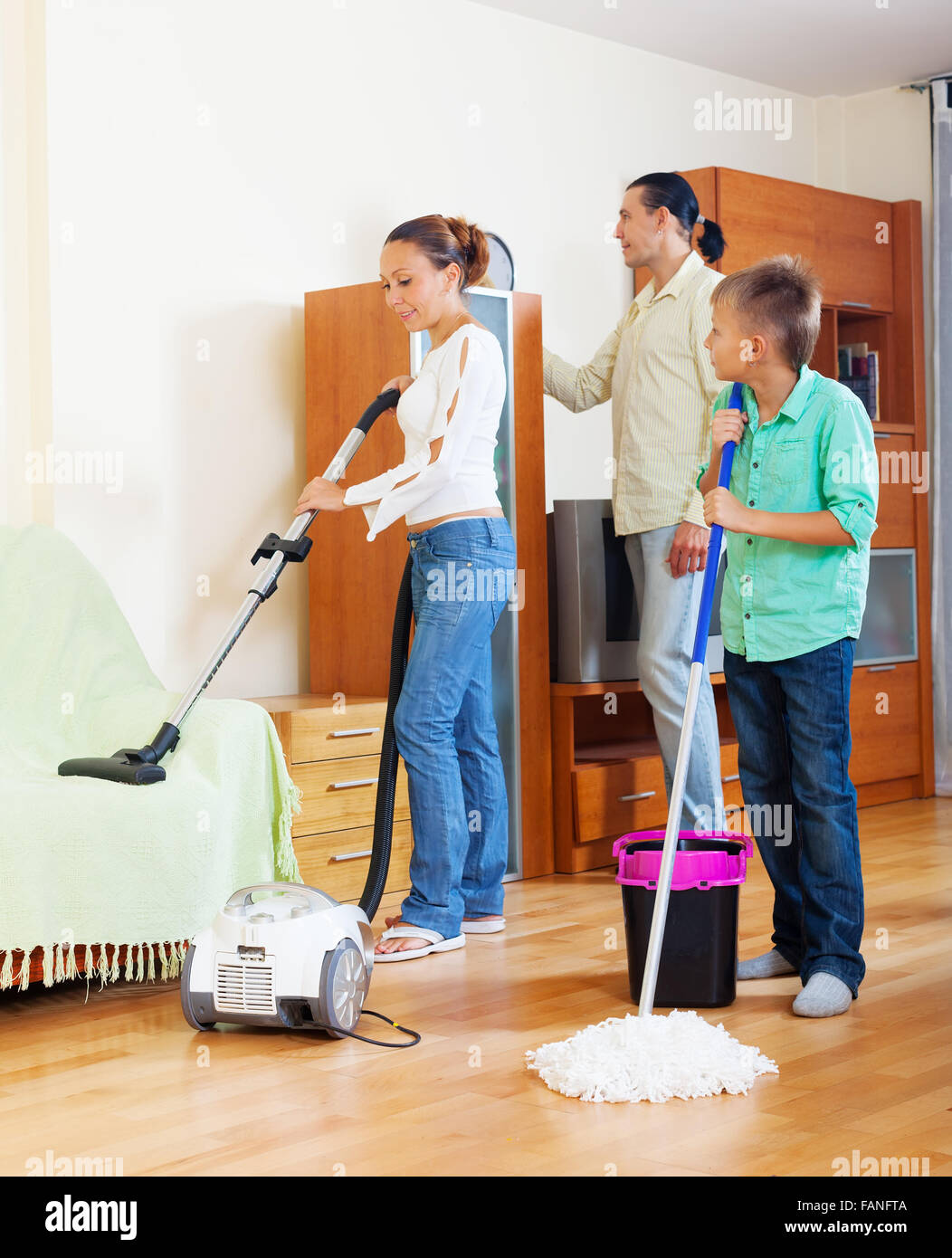 family of three with teenager doing housework together in living room ...