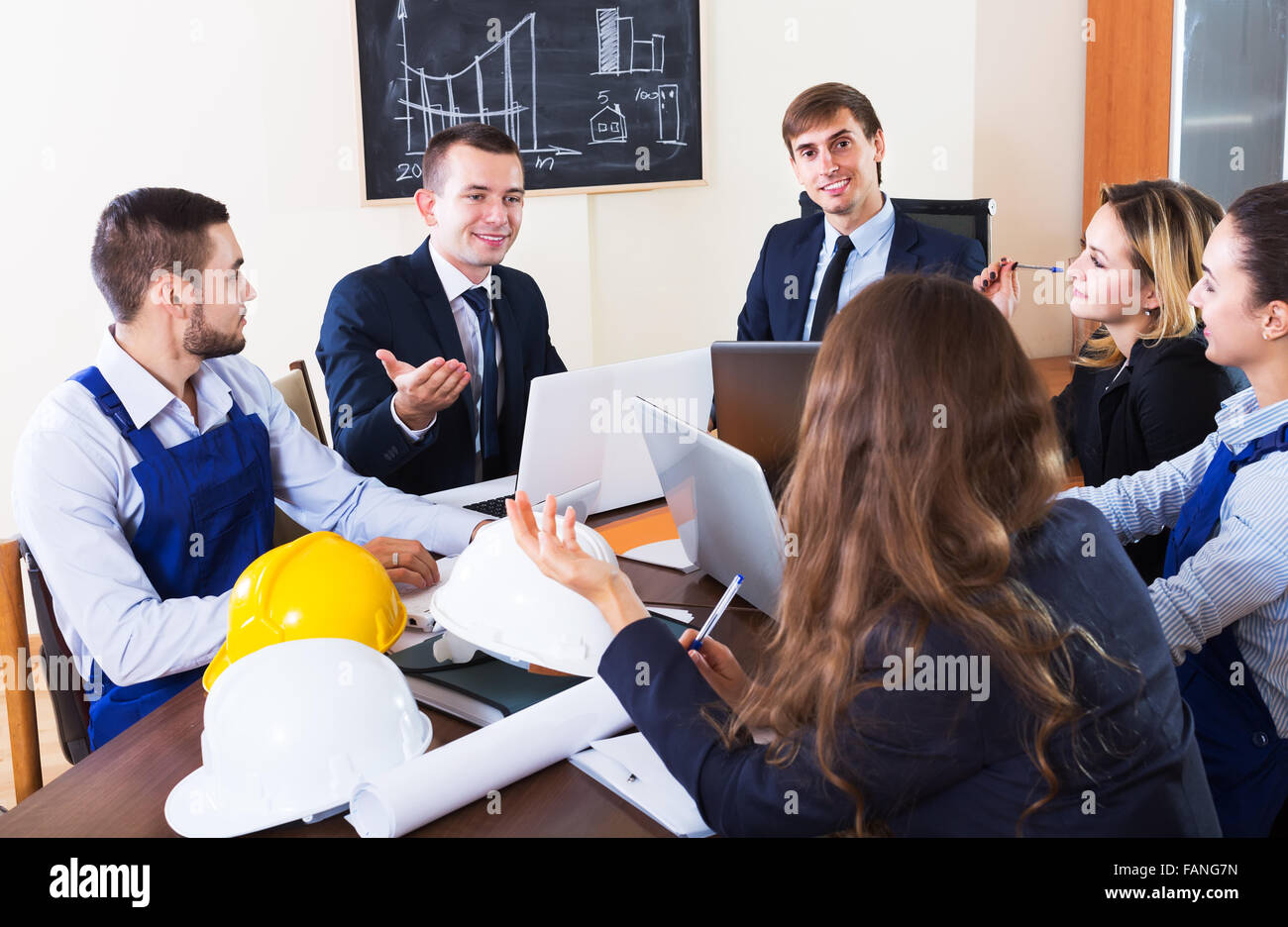 Team of young positive professionals with helmets and laptops on the ...
