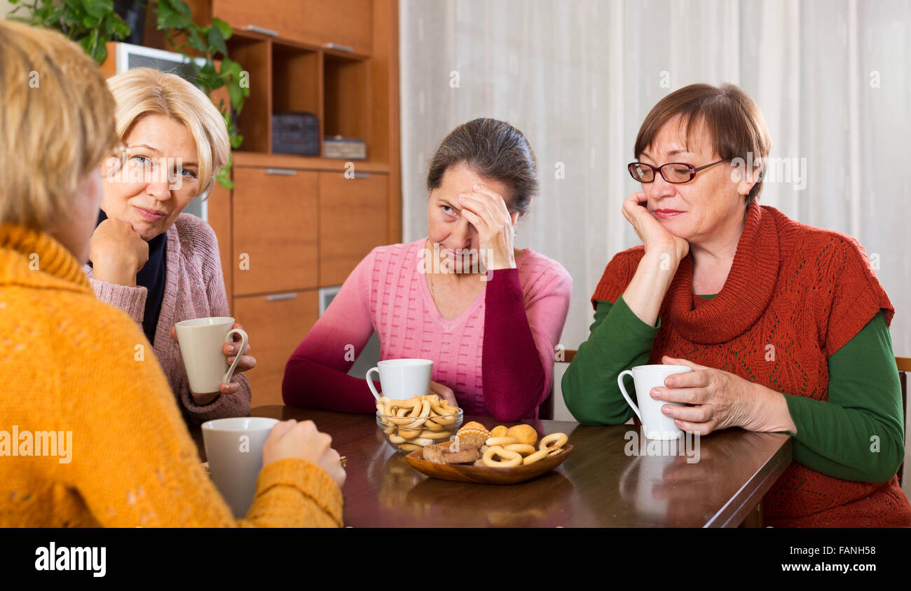 sad senior female friends drinking tea and sharing problems at table ...
