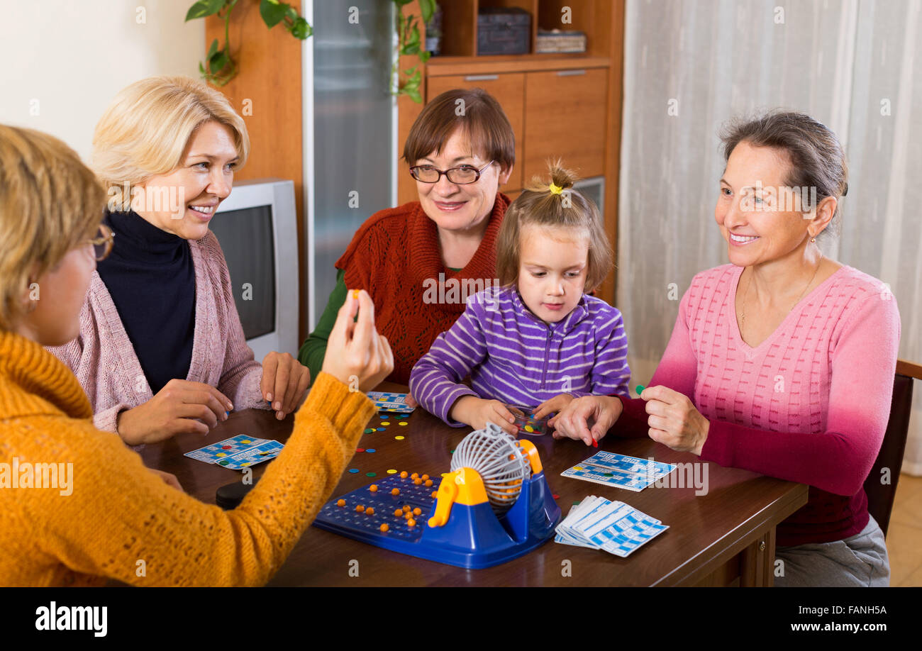 Positive senior female friends with child sitting at desk with bingo ...