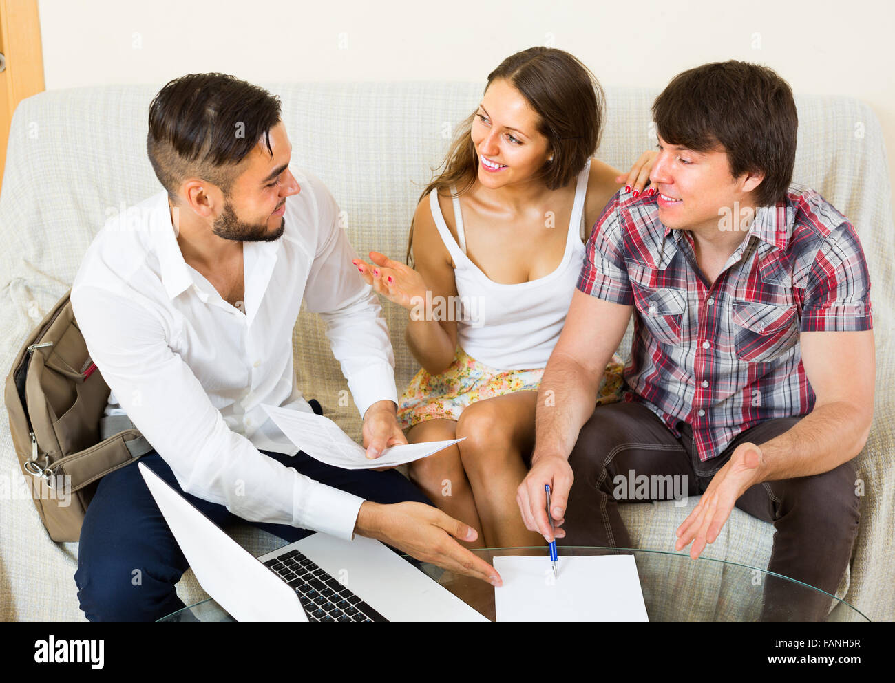 Happy salesman and smiling young couple talking about purchase at their ...