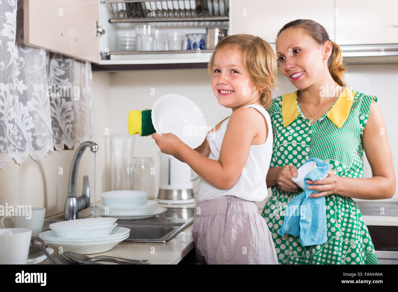 Smiling baby girl helping mother washing dishes in the kitchen. Focus ...