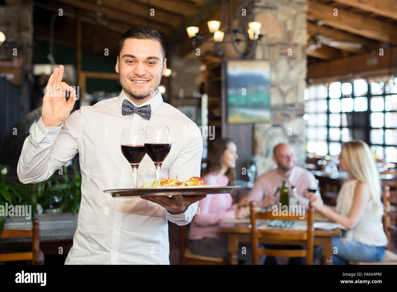 Handsome waiter in a white shirt wearing a bowtie showing ok sign in a ...