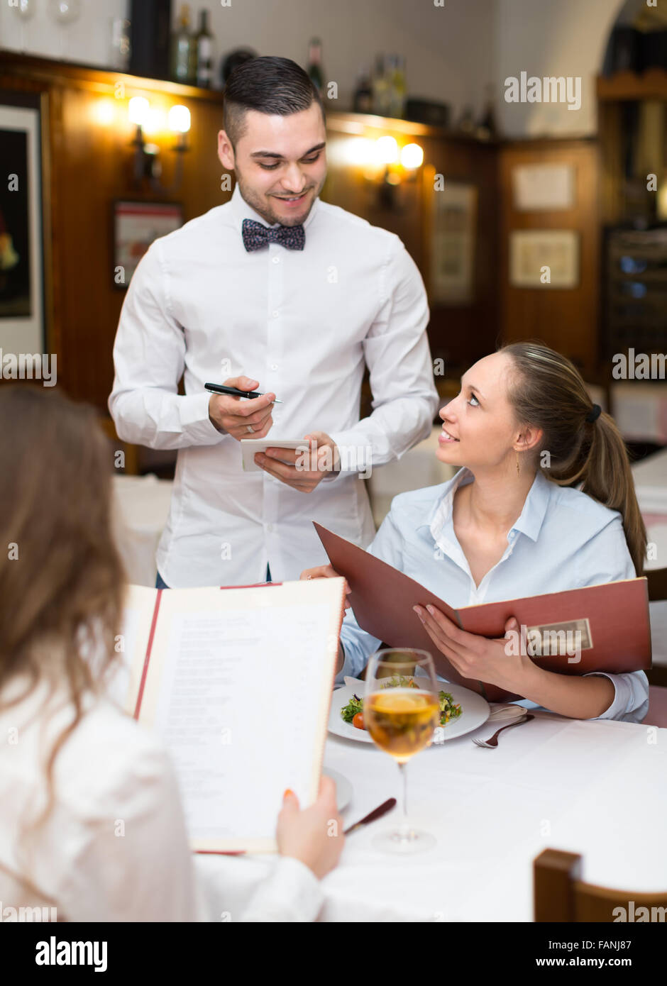 Young smiling waiter offering tasty dishes to guests at cafe. Selective ...