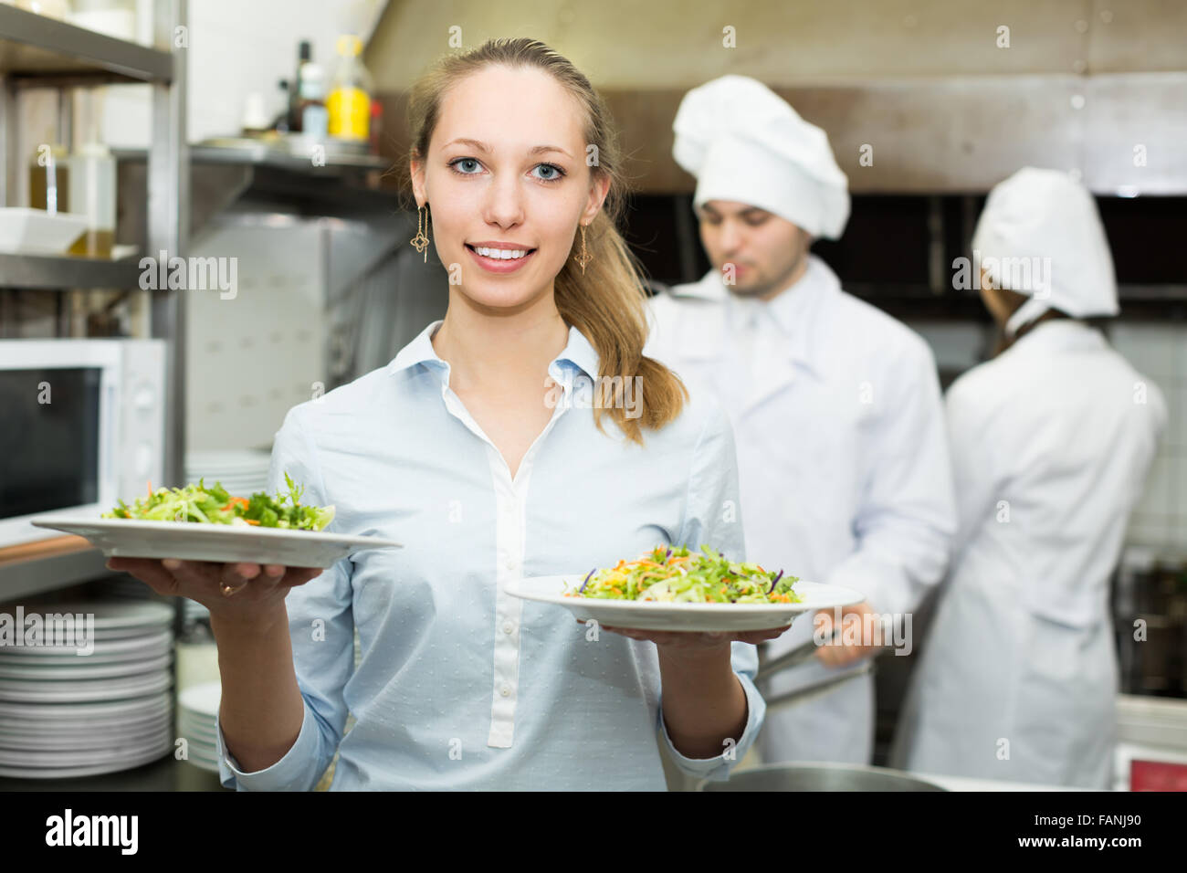 Smiling blonde young waitress taking dish from kitchen Stock Photo - Alamy