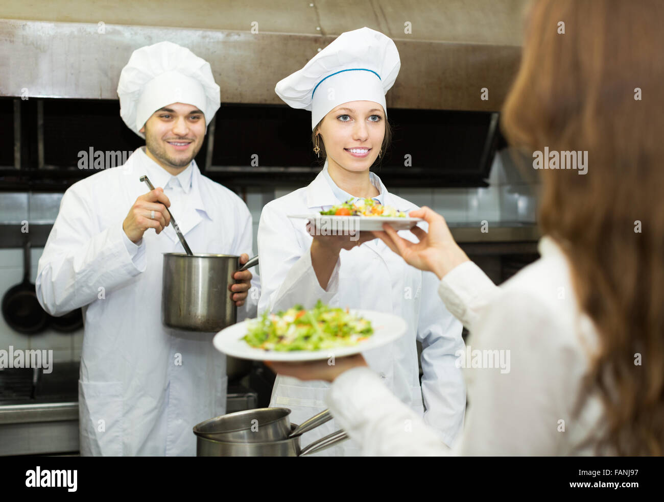 Positive cook gives to female waitress plates with prepared meal at ...
