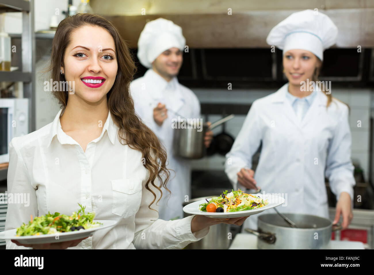 Two chefs and young female waiter at restaurant kitchen. Selective ...
