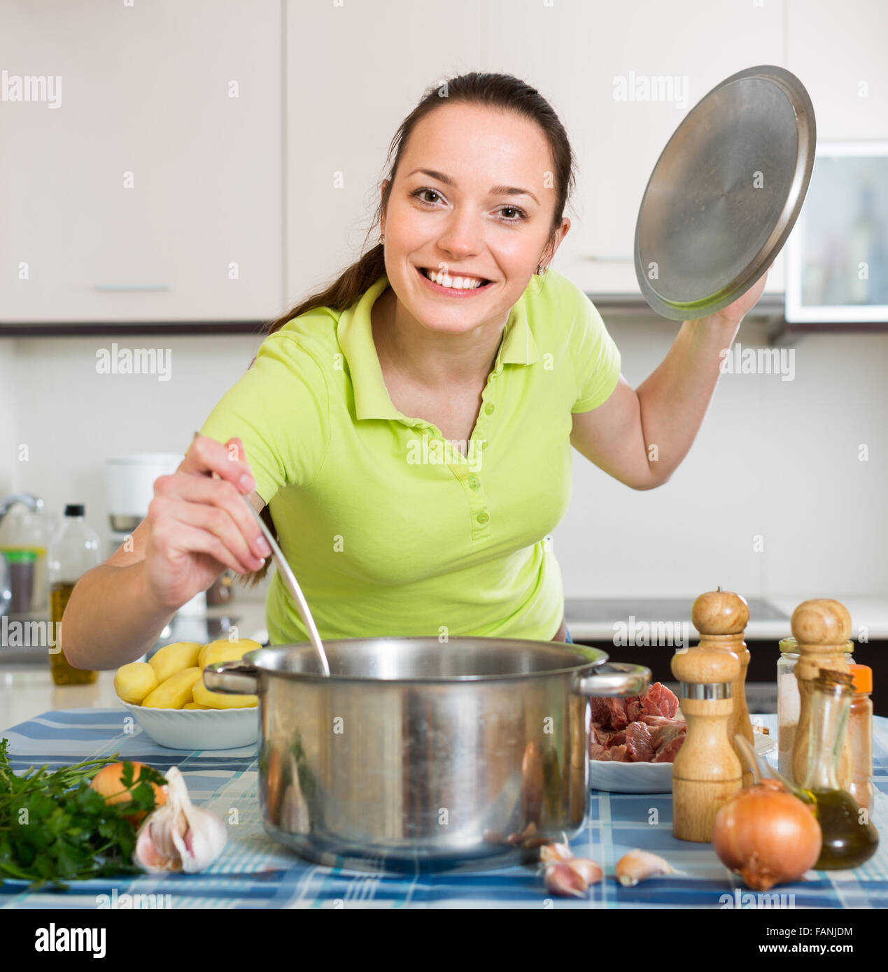 Cheerful smiling young woman cooking with meat and potatoes at kitchen ...
