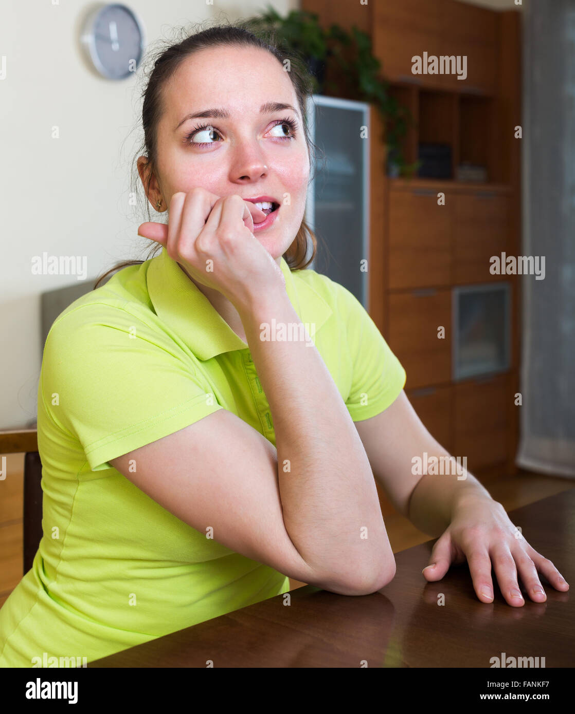 Young woman sitting at table and biting nails indoors Stock Photo - Alamy