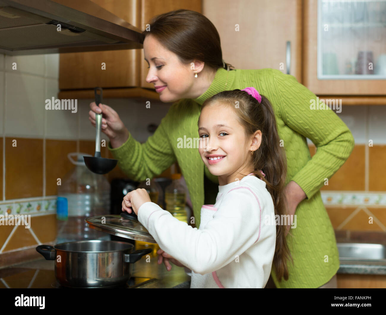 Smiling mother and daughter preparing soup together at domestic kitchen ...