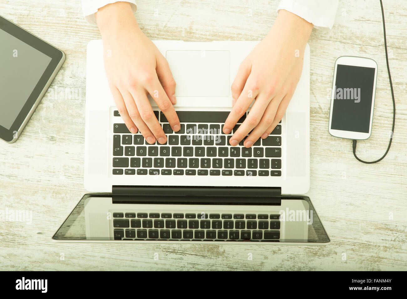 A young man using his laptop computer and various other devices on a ...