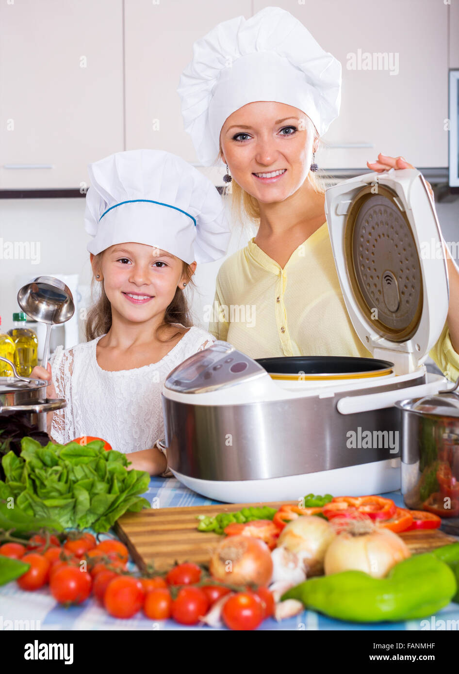 Positive mother and little girl preparing vegetables in slow-cooker ...