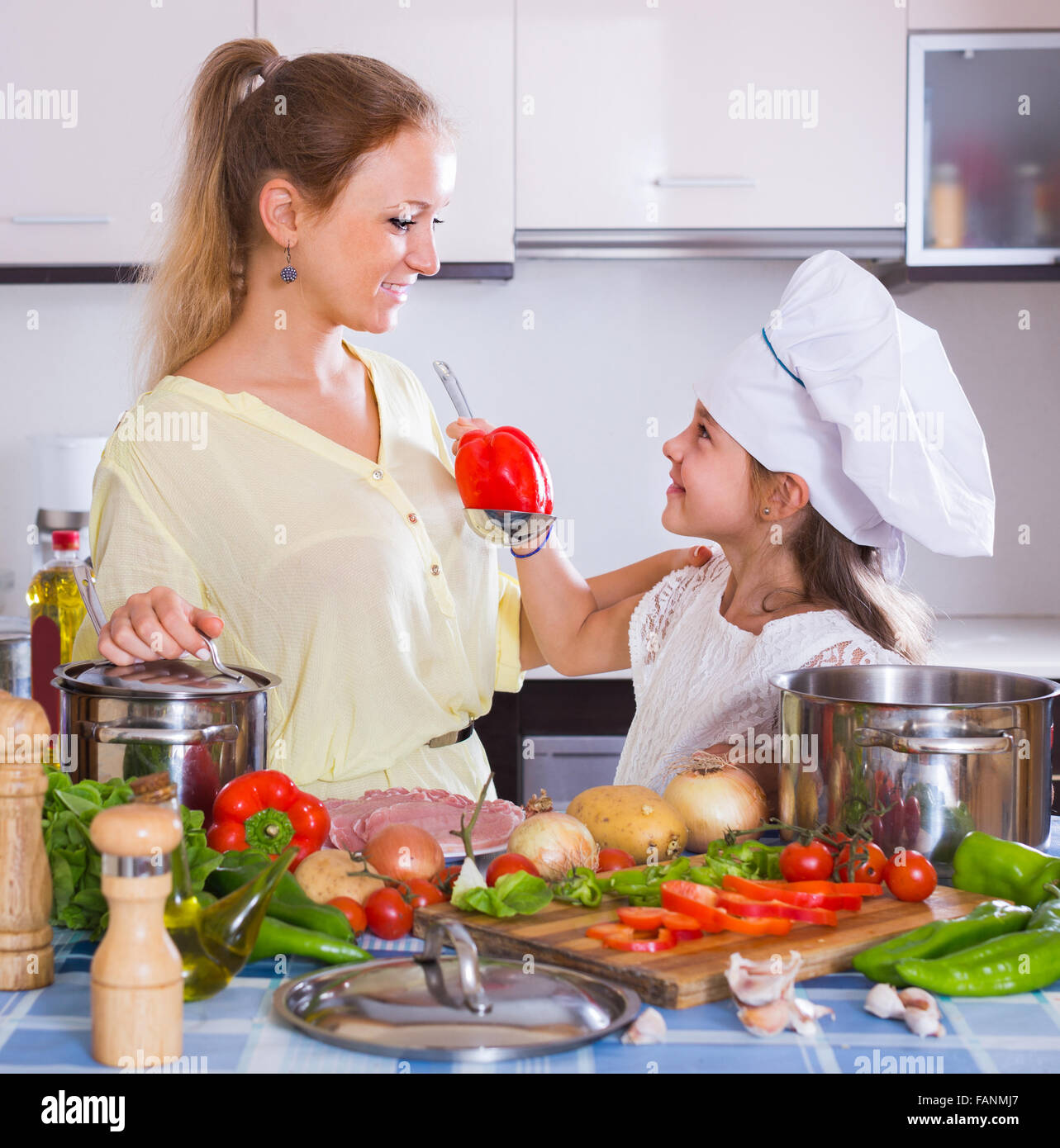 young european mom and little daughter cooking vegeterian dish indoors ...