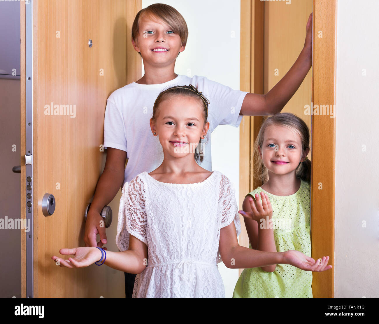 Three happy children standing at house entrance and smiling Stock Photo ...