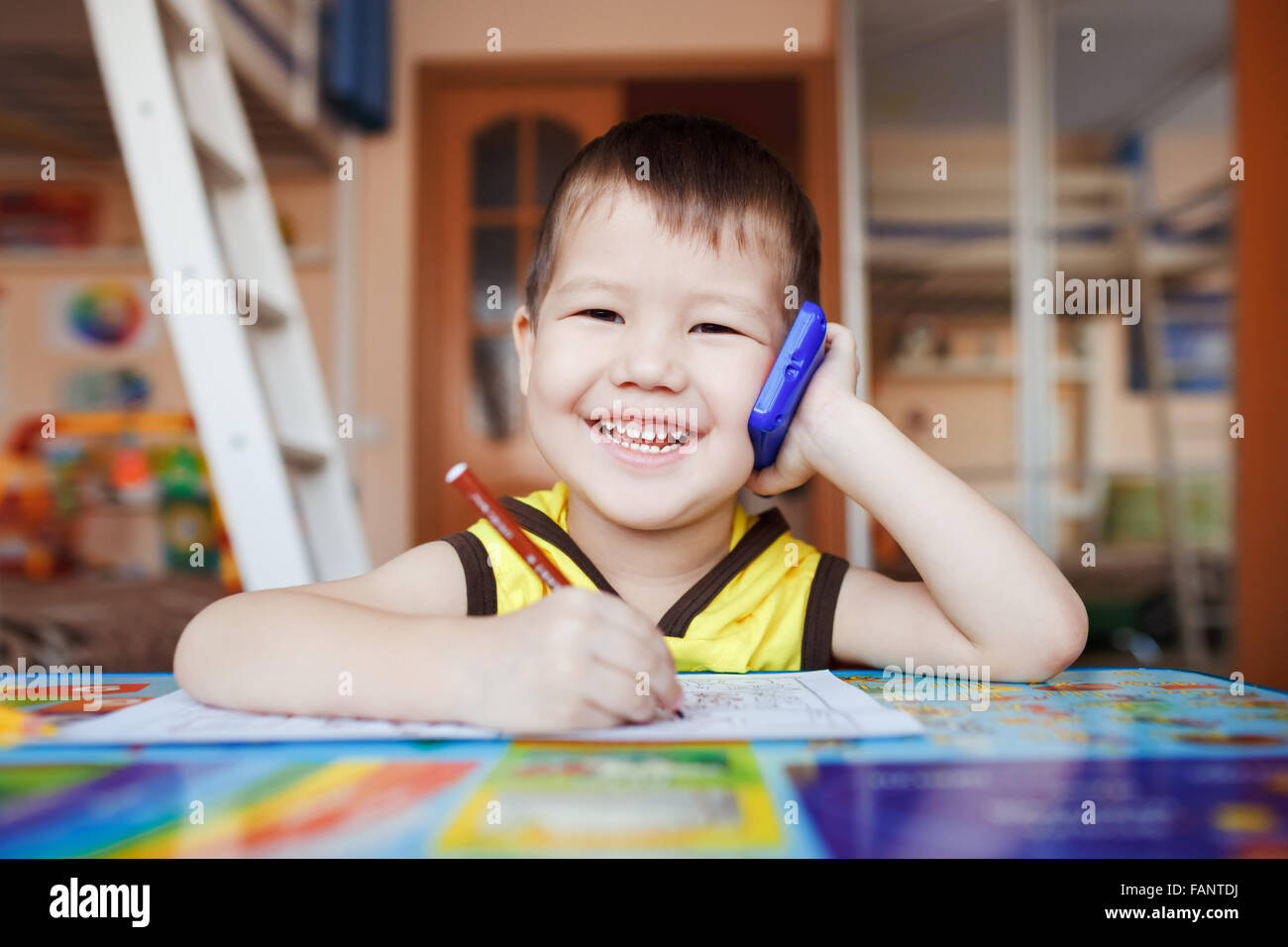 Happy little boy talking on smartphone at home while writing letters ...