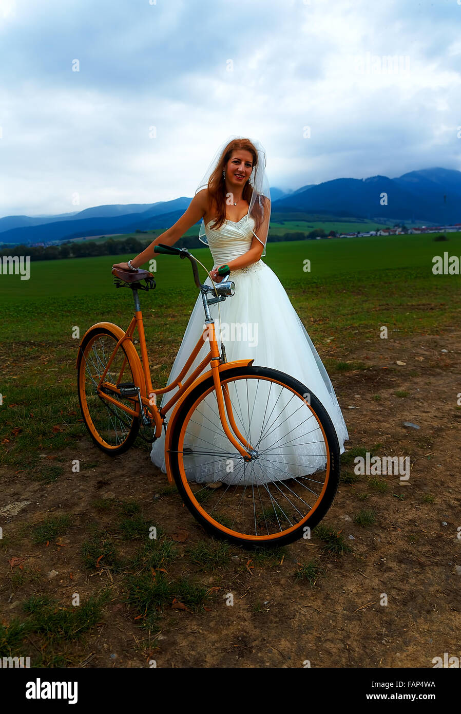 bride on orange bike in beautiful wedding dress with lace in landscape ...