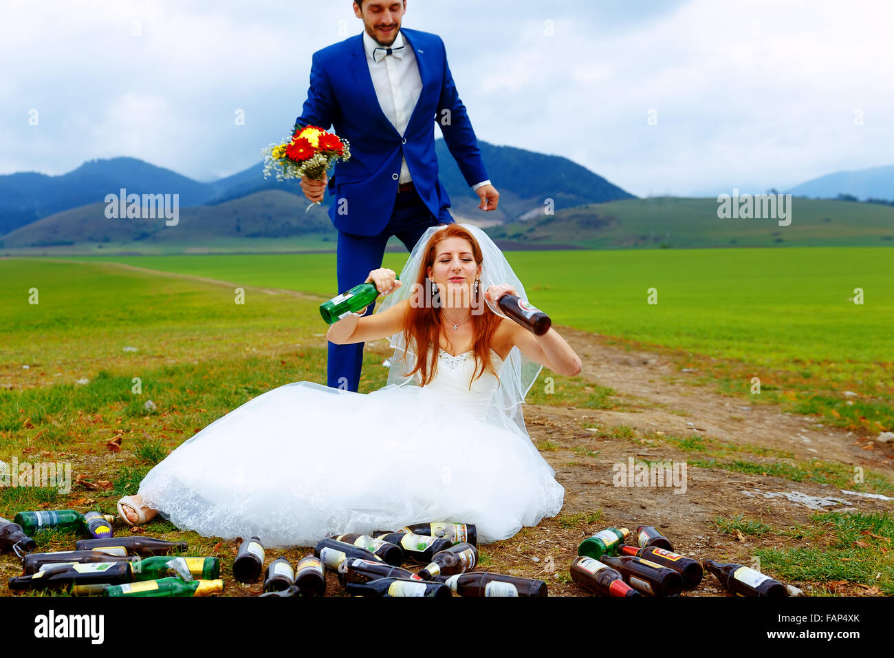 drunken bride with lots of empty beer bottles in mountain landscape and groom racing to her ...