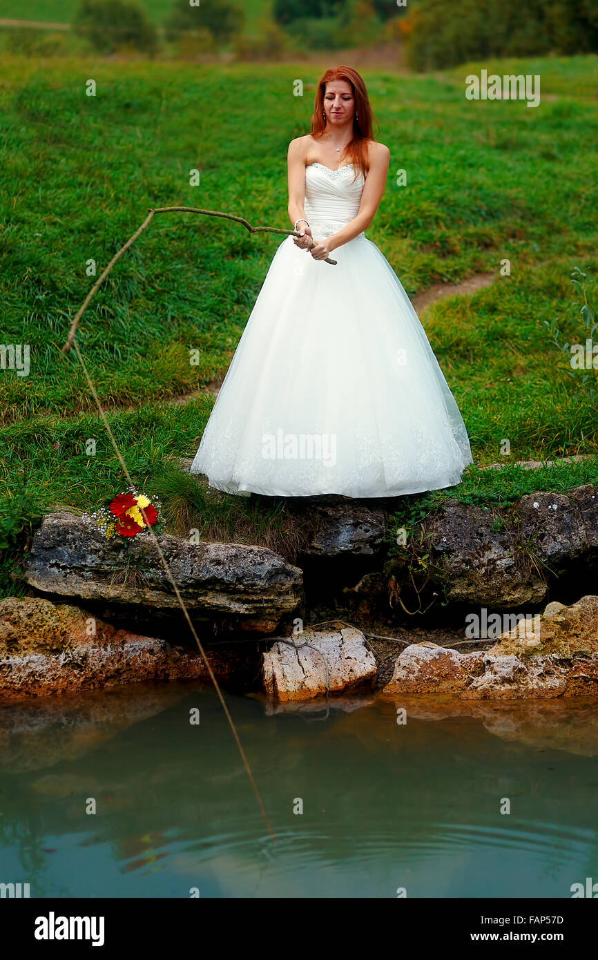 bride in dress with fishing rod sitting by a lake trying to catch a ...