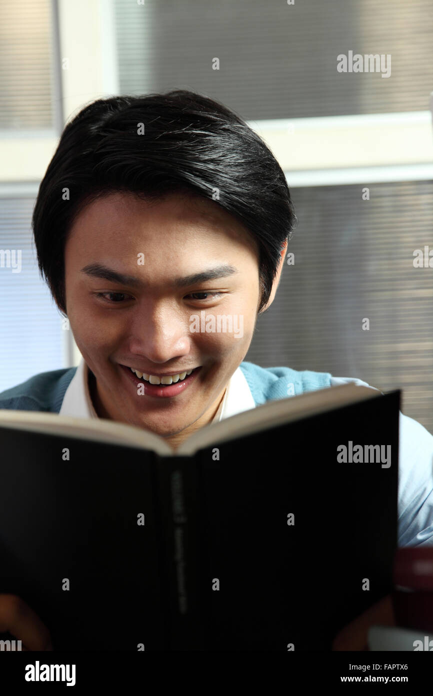 Young man reading by piled books Stock Photo - Alamy