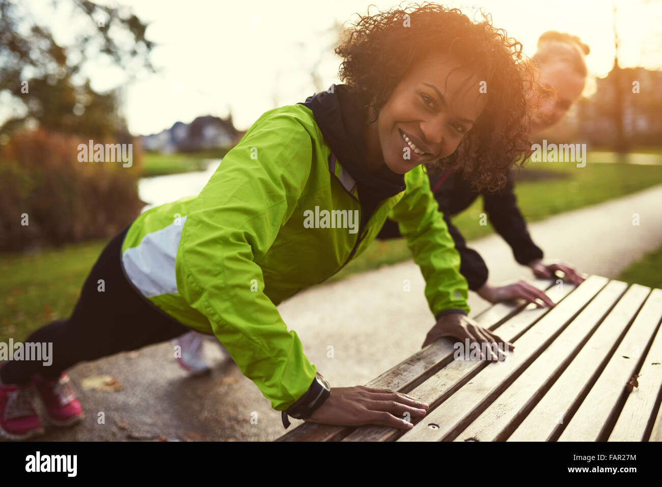 Two smiling sportswomen doing push-ups using bench in park Stock Photo ...