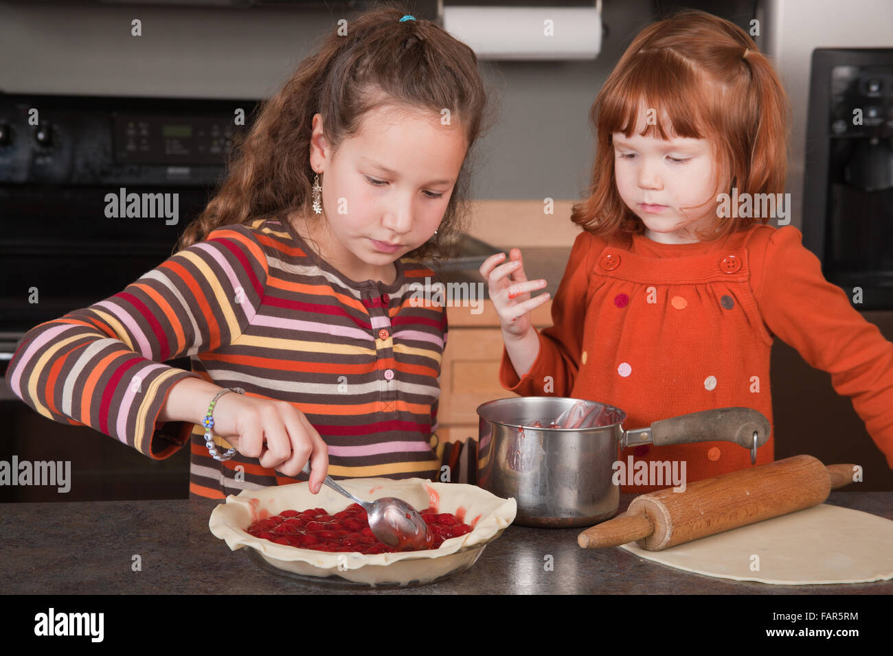 Two sisters adding cherry pie filling to pie crust Stock Photo - Alamy