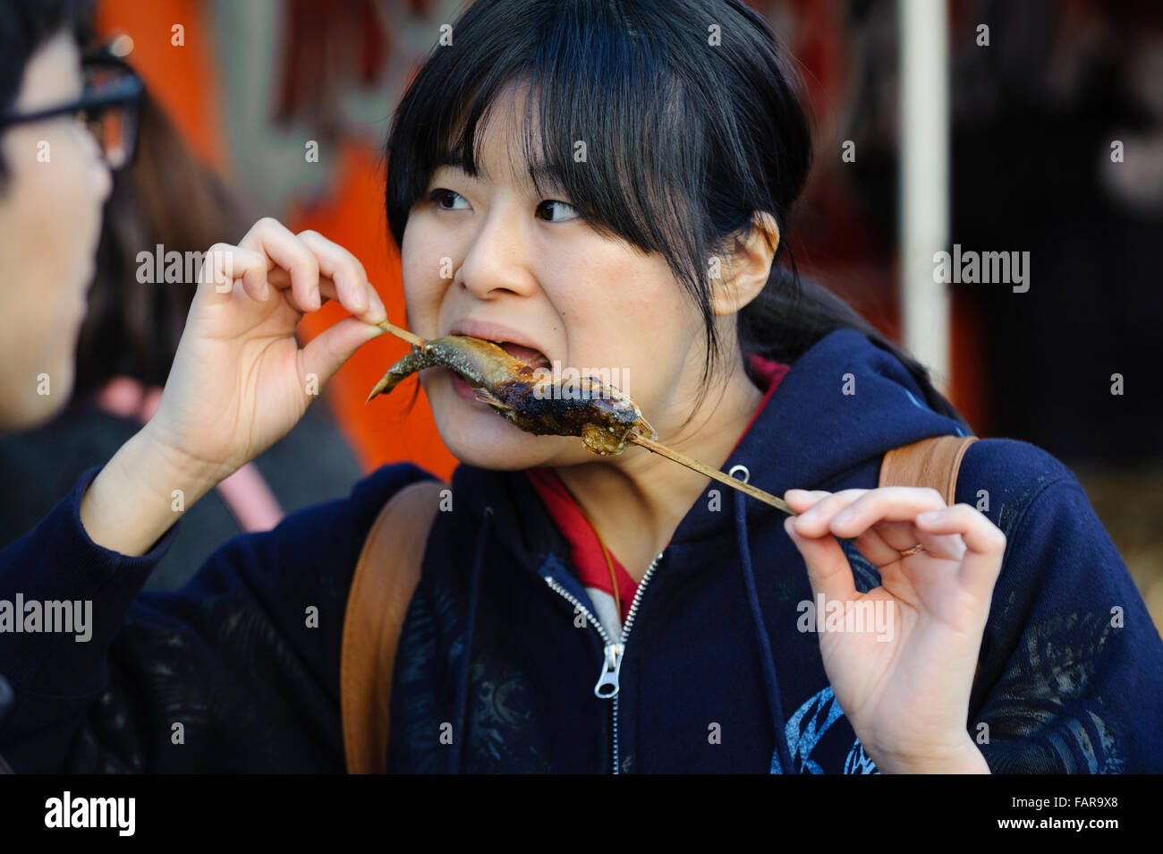 JANUARY 3, 2016 - A woman eats grilled fish on a stick on Nakamise-dori ...