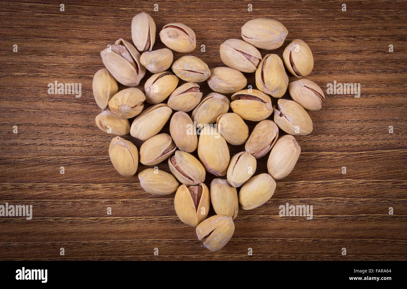 Heart shaped roasted pistachio nuts on natural wooden table background ...