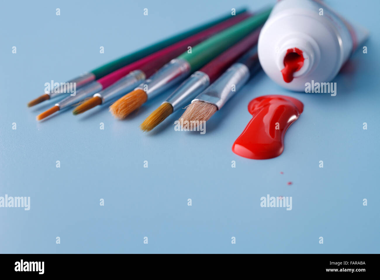 Multiple paintbrushes with a tube of paint isolated on blue background ...
