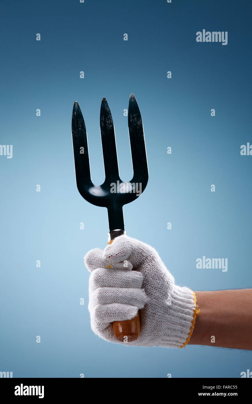 Hand holding garden pitchfork on coloured background Stock Photo - Alamy