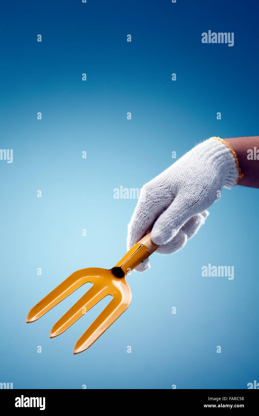 Hand holding garden pitchfork on coloured background Stock Photo - Alamy