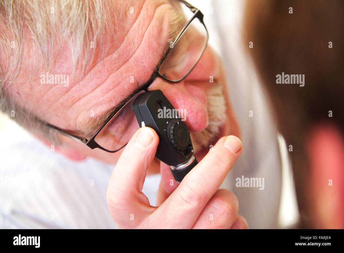 White male GP doctor uses an Ophthalmoscope to check patient eyes ...
