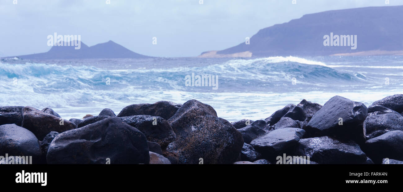 Black rock stone coast in front of rough windy sea with waves on cape ...