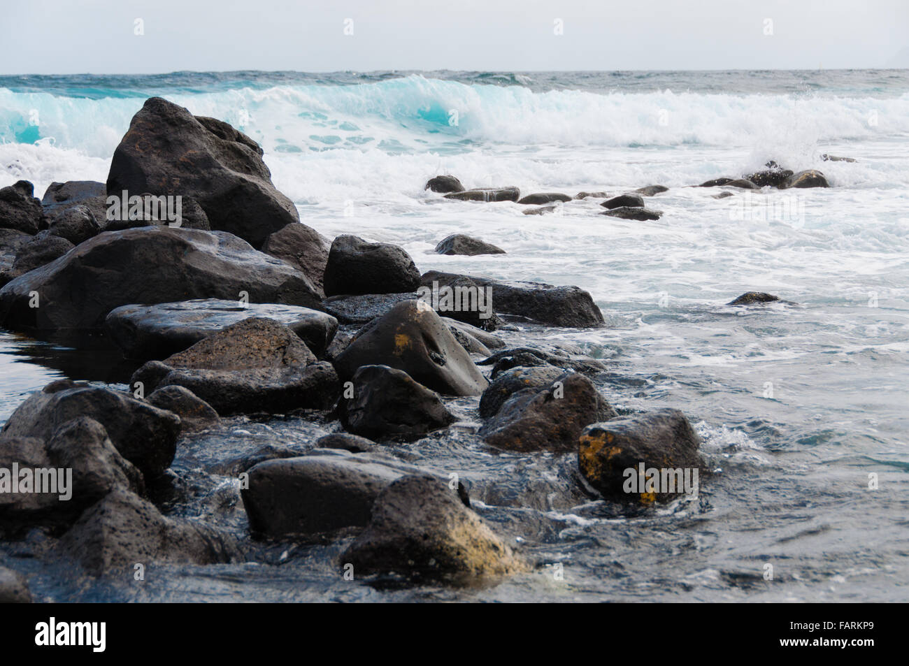 Black rock stone coast in front of rough windy sea with waves on cape ...