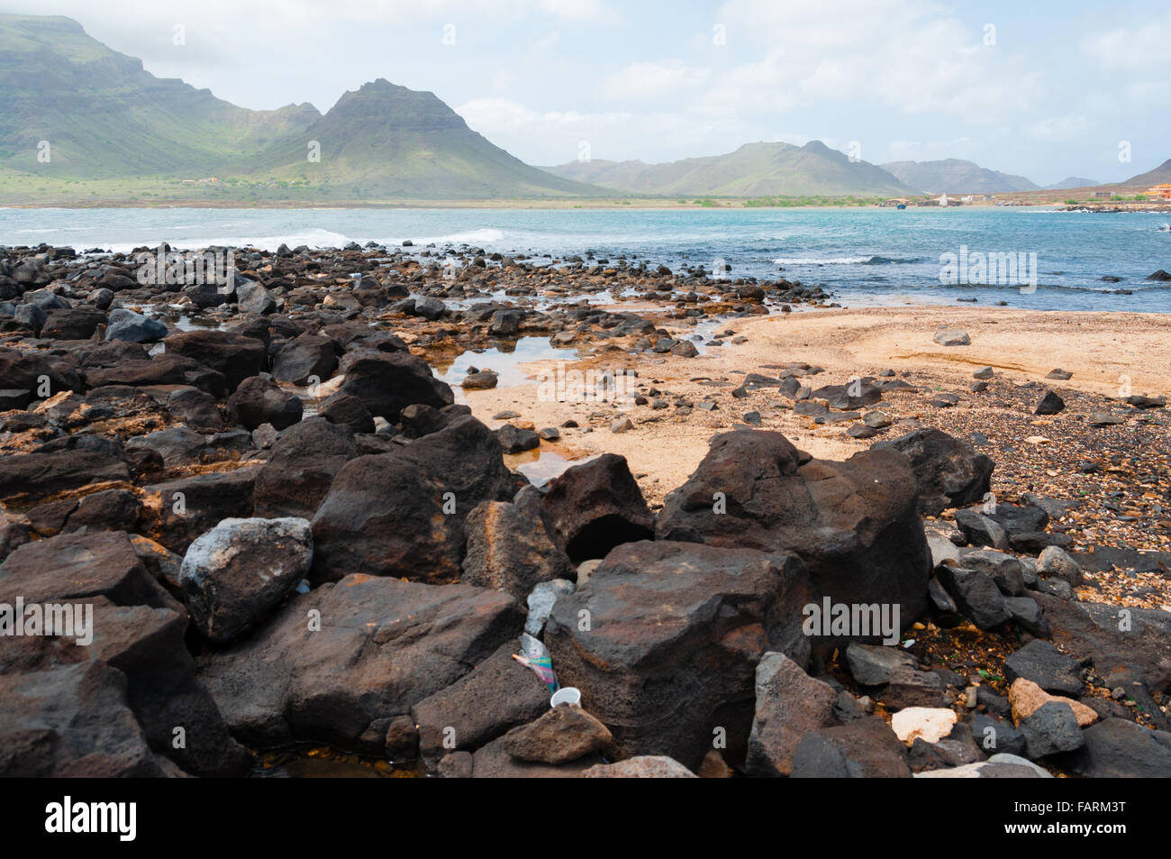 Black rock stone sand beach coast in front of blue sea with mountain ...