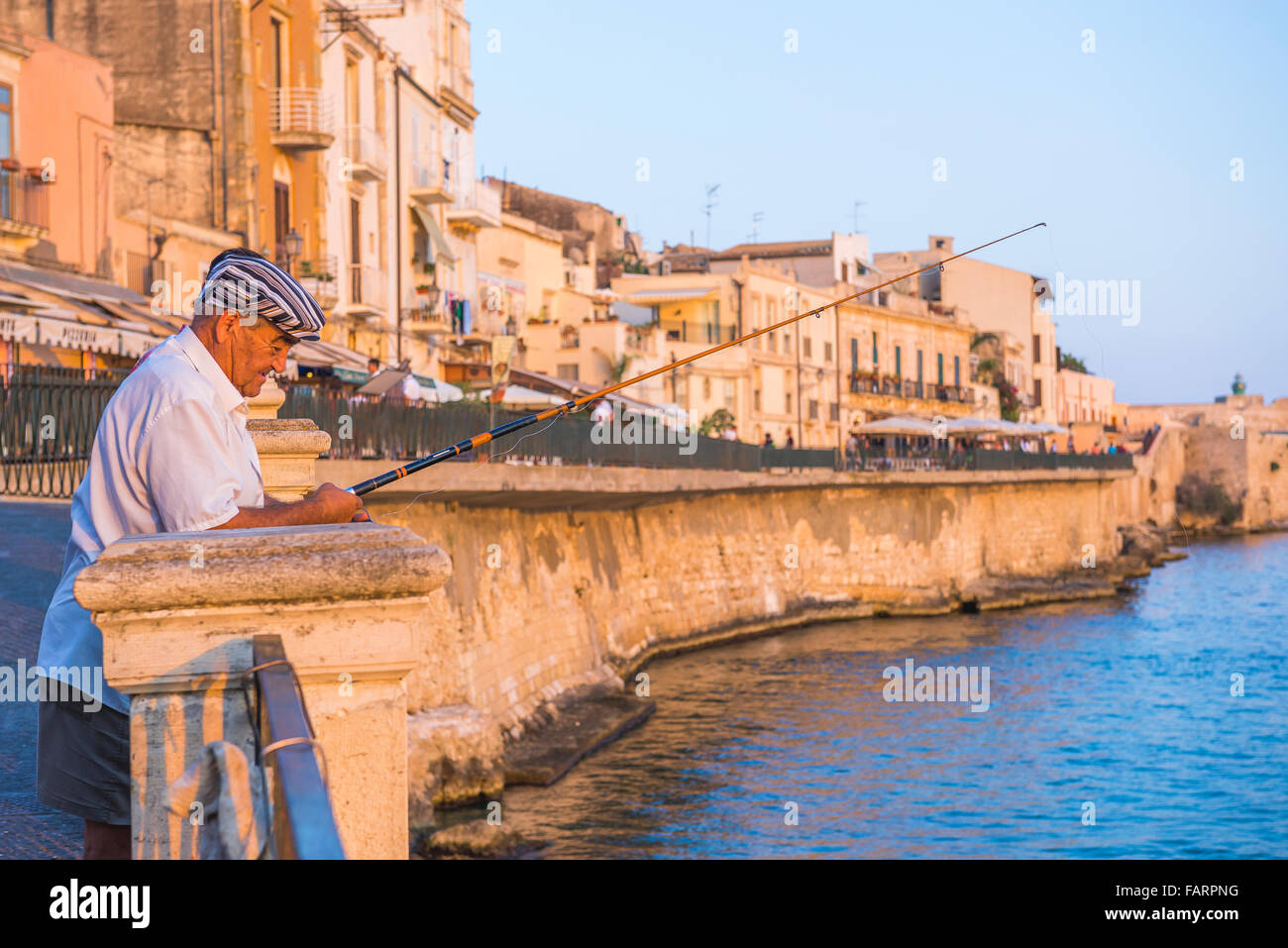 Fishing Sicily, view of a senior man fishing from the high sea wall ...