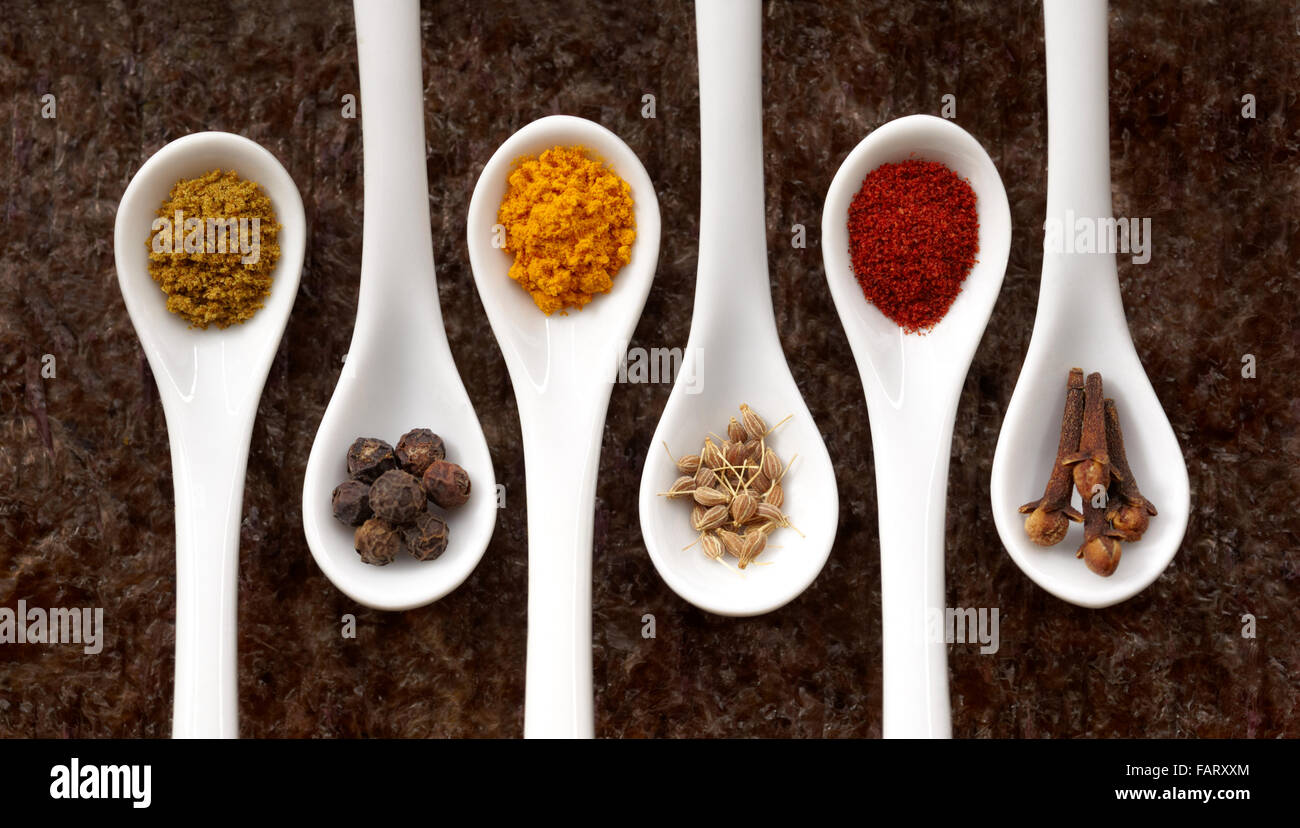 Five white spoons with assorted spices on a dark background Stock Photo ...