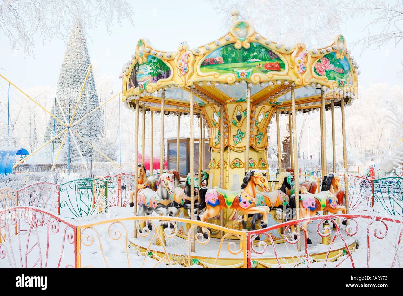Merry-go-round with traditional horses covered with snow. Behind the ...