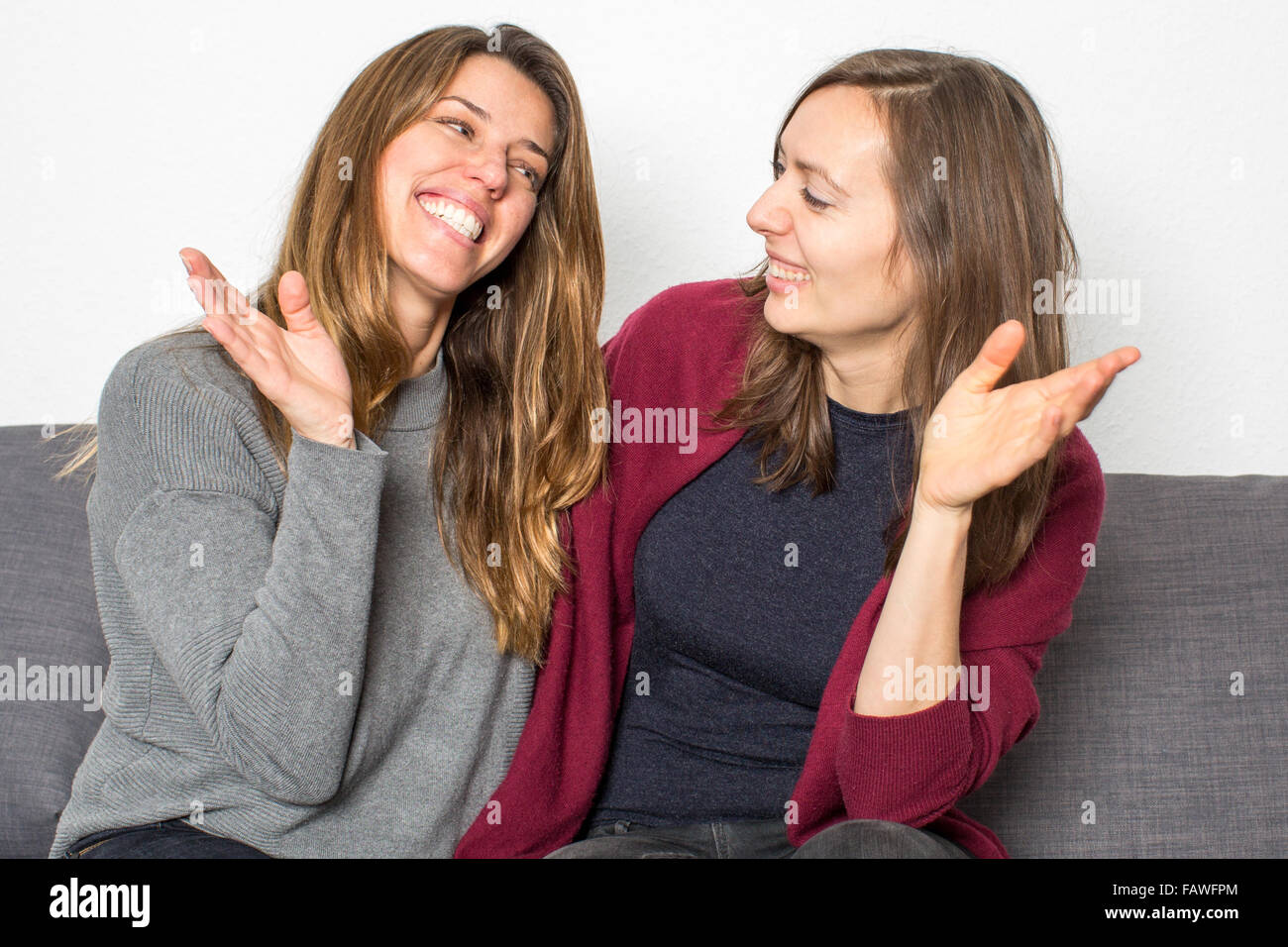 Two female friends having fun while sitting on coach in the living room ...