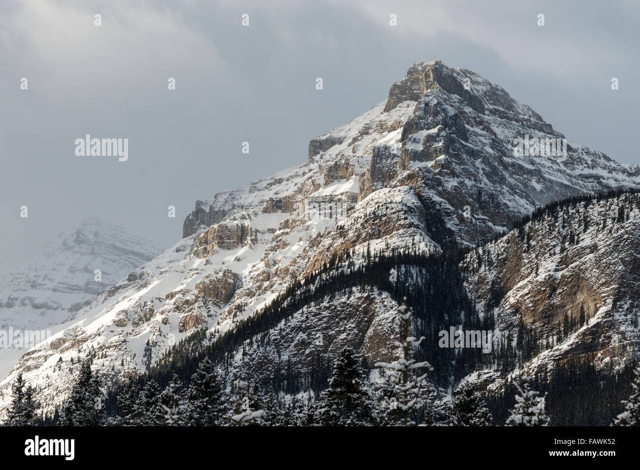 Rugged mountain peak with snow under a cloudy sky; Lake Louise, Alberta ...