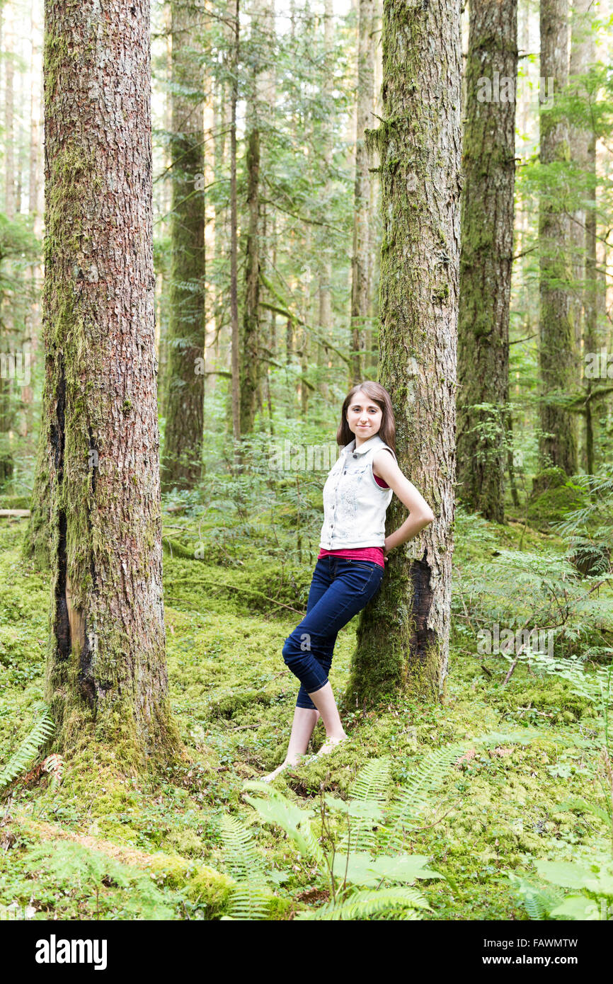Portrait of a teenage girl leaning against a tree in a forest ...