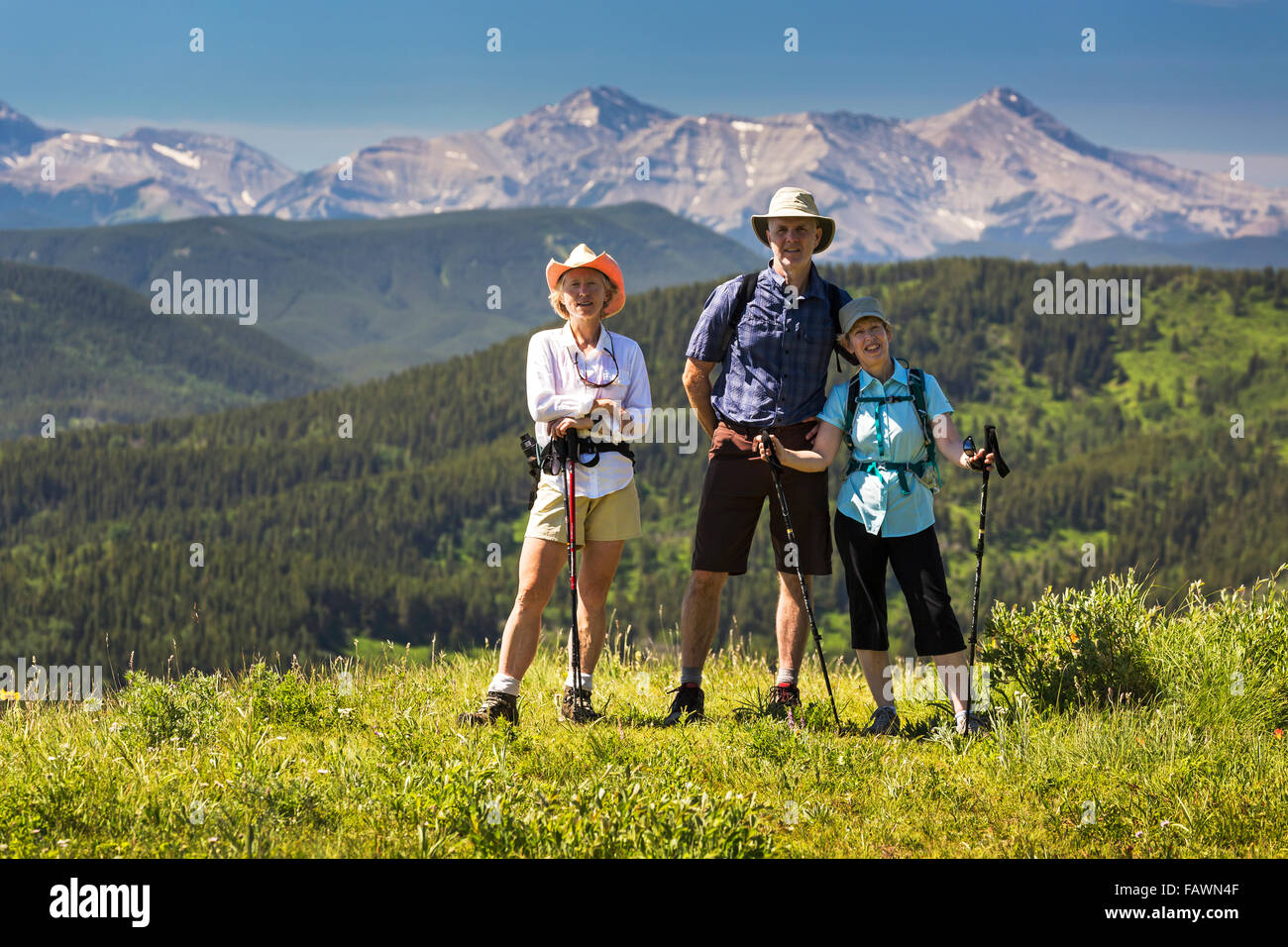 Three hikers, two female and one male, on top of grassy hill with ...